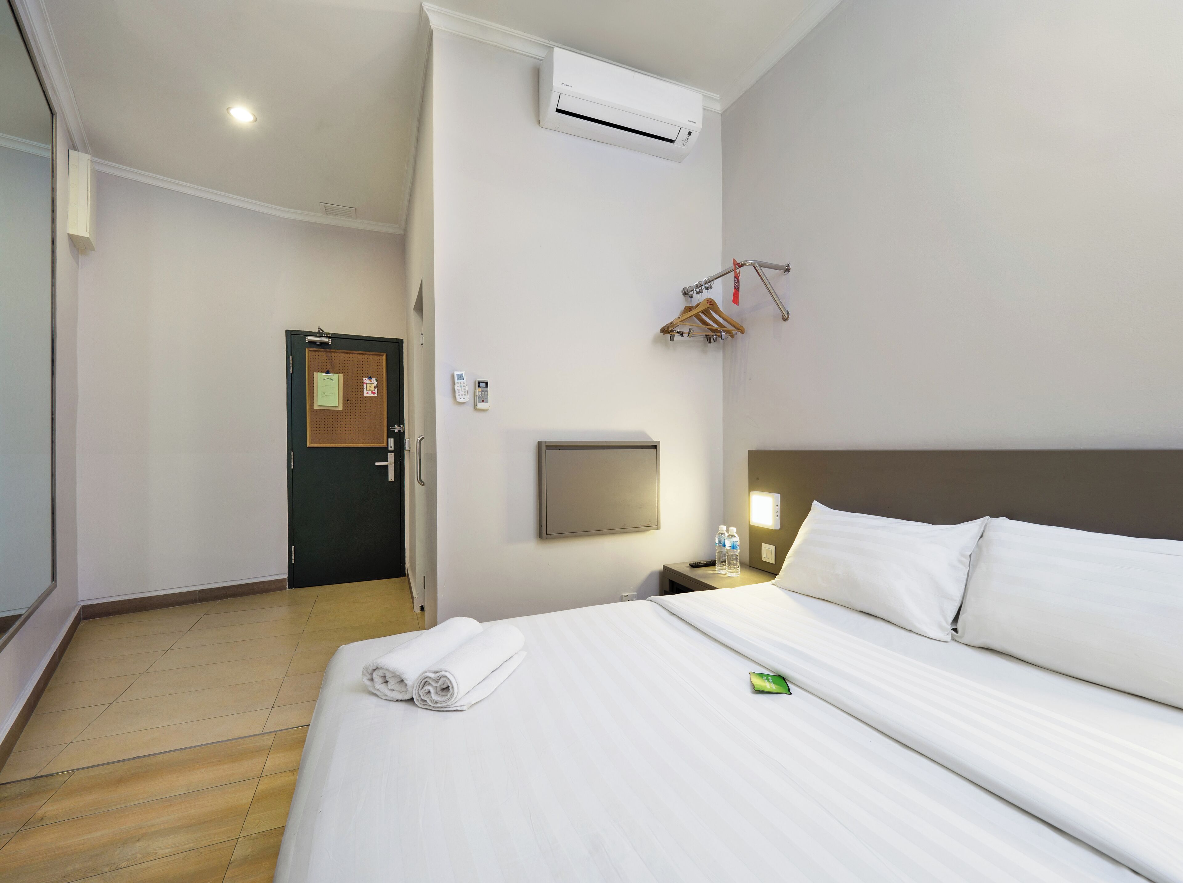 Quarto de hotel com cama, mesa de cabeceira com abajur, TV na parede e aparelho de ar condicionado.