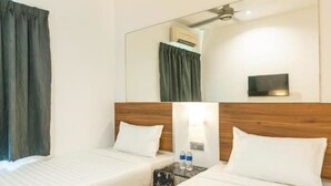 Quarto de hotel com duas camas, um ventilador de teto, um aparelho de ar condicionado, uma mesa de cabeceira com abajur e um espelho grande na parede.