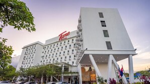 Edifício Tune Hotels com um letreiro vermelho chamativo, vários andares e área de estacionamento com diversos carros.