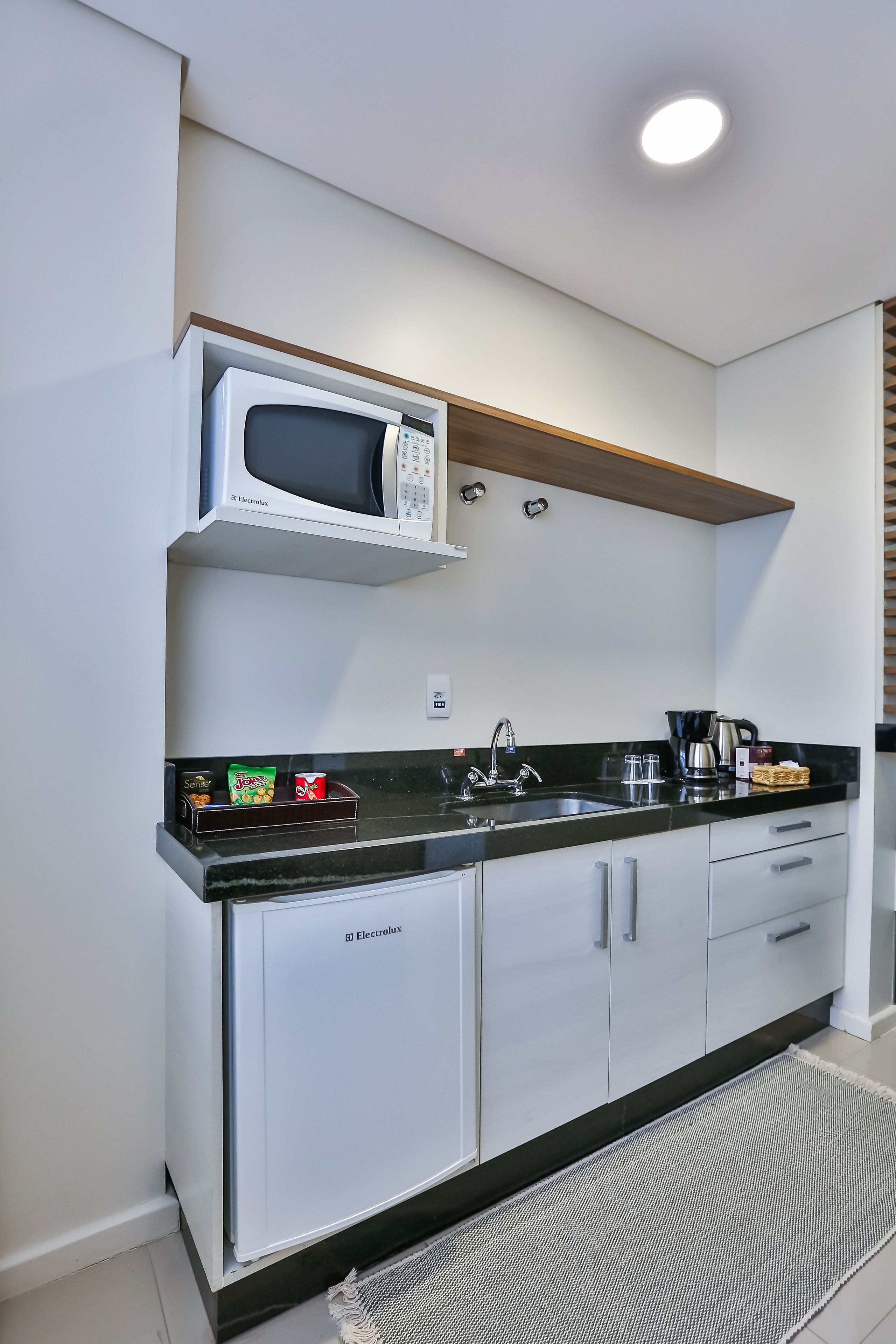 Uma cozinha compacta com micro-ondas branco, frigorífico Electrolux e bancada preta.