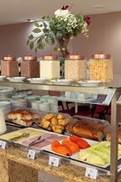 Buffet com diversos alimentos, incluindo pães, doces e frutas.
