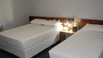 Quarto de hotel com duas camas de solteiro, uma mesinha de cabeceira com abajur, telefone e um pequeno vaso com flores.