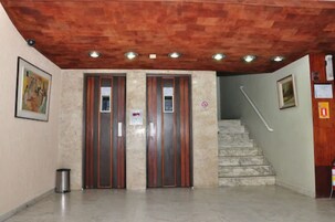 Um saguão com duas portas de madeira, uma escada e uma lixeira.