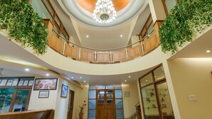 Um interior espaçoso, em vários níveis, com uma escadaria imponente, balaústres de madeira e um candelabro.