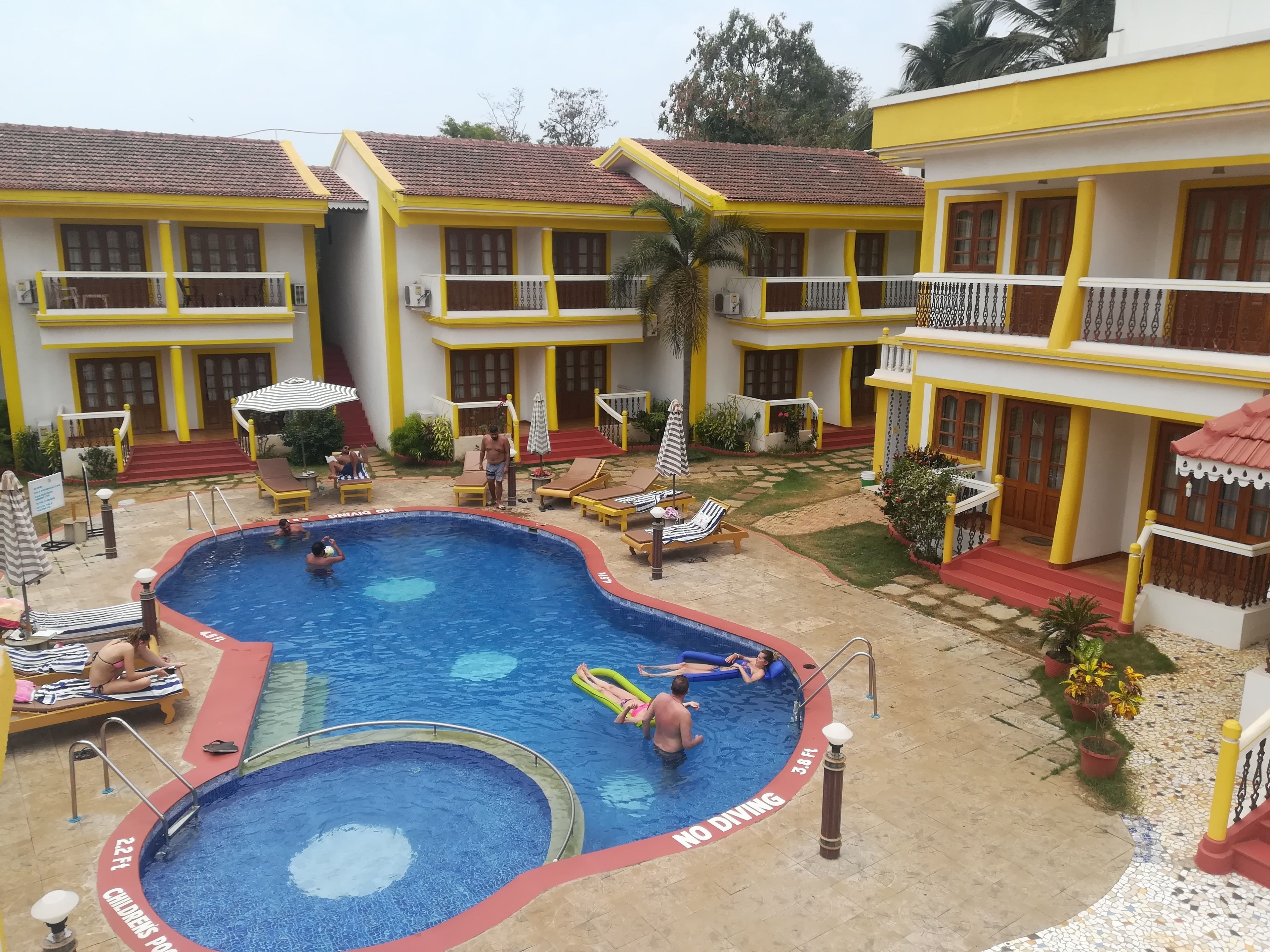 Piscina rodeada por edifícios amarelos e brancos com varandas, piscina infantil e espreguiçadeiras.