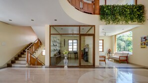 Uma sala de estar ampla com escada de madeira, uma grande porta de vidro que dá para a cozinha e vista para o exterior.