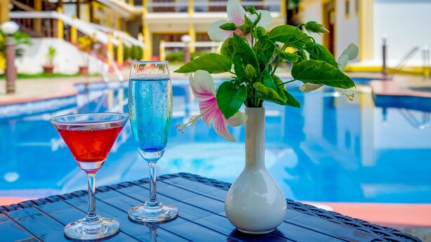 Um espaço junto à piscina com vista clara para a piscina, área de bar com duas bebidas e um vaso de planta.