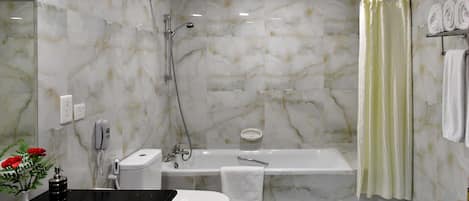 Uma casa de banho com parede de mármore, banheira, sanita, lavatório e chuveiro.
