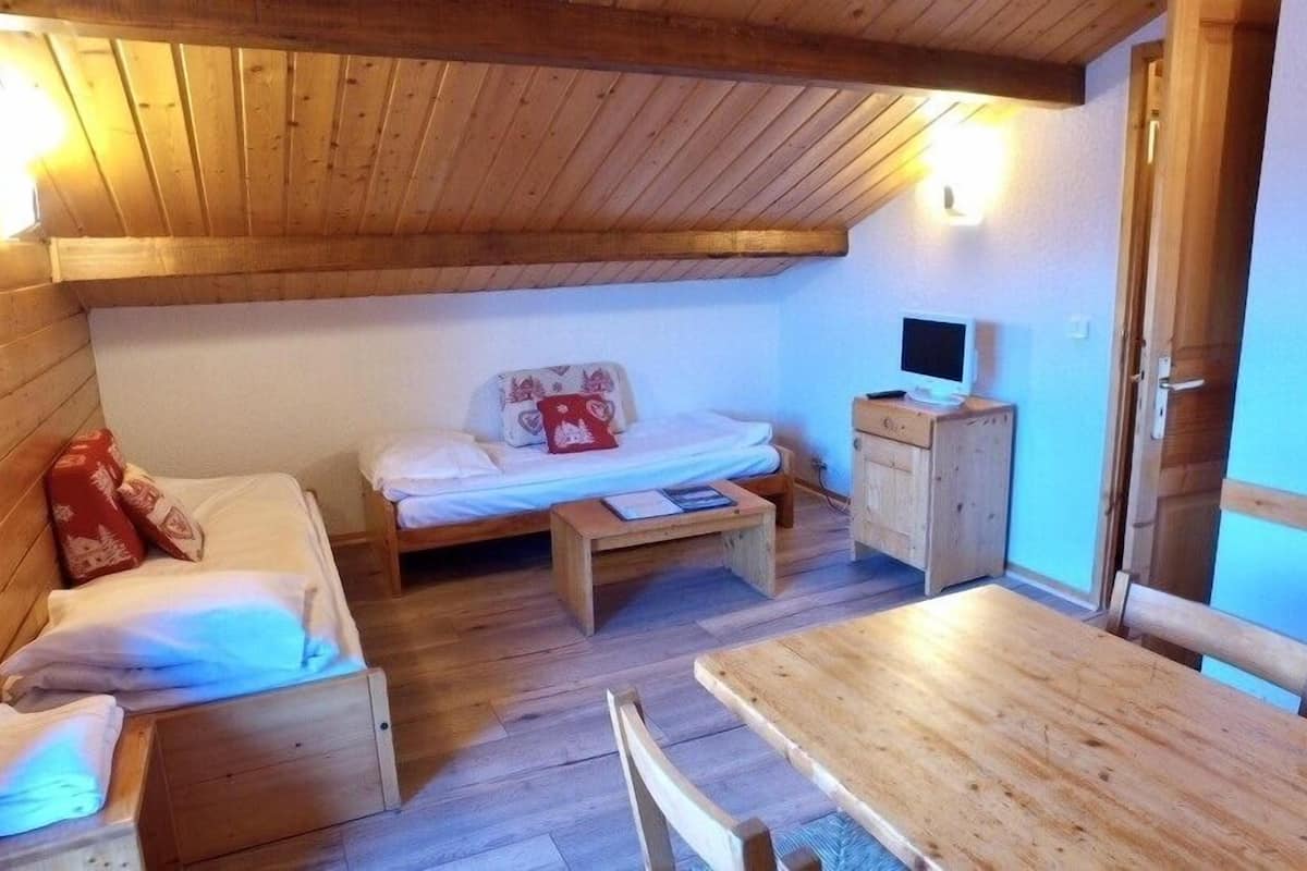 Uma cabana aconchegante com cama no mezanino, uma pequena escrivaninha com computador e uma mesa de jantar.