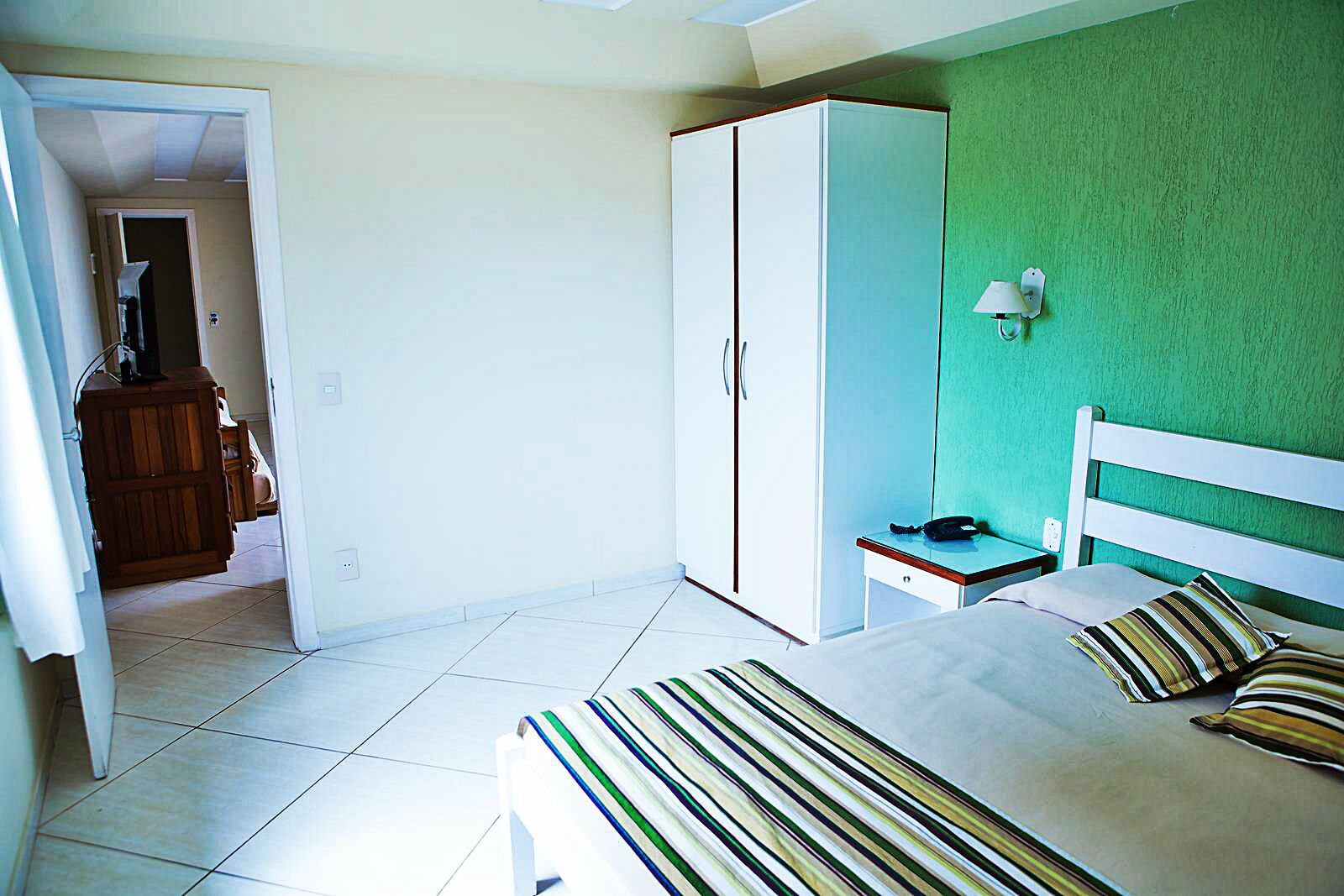 Quarto com uma cama, um guarda-roupa, uma mesa de cabeceira e uma parede verde.