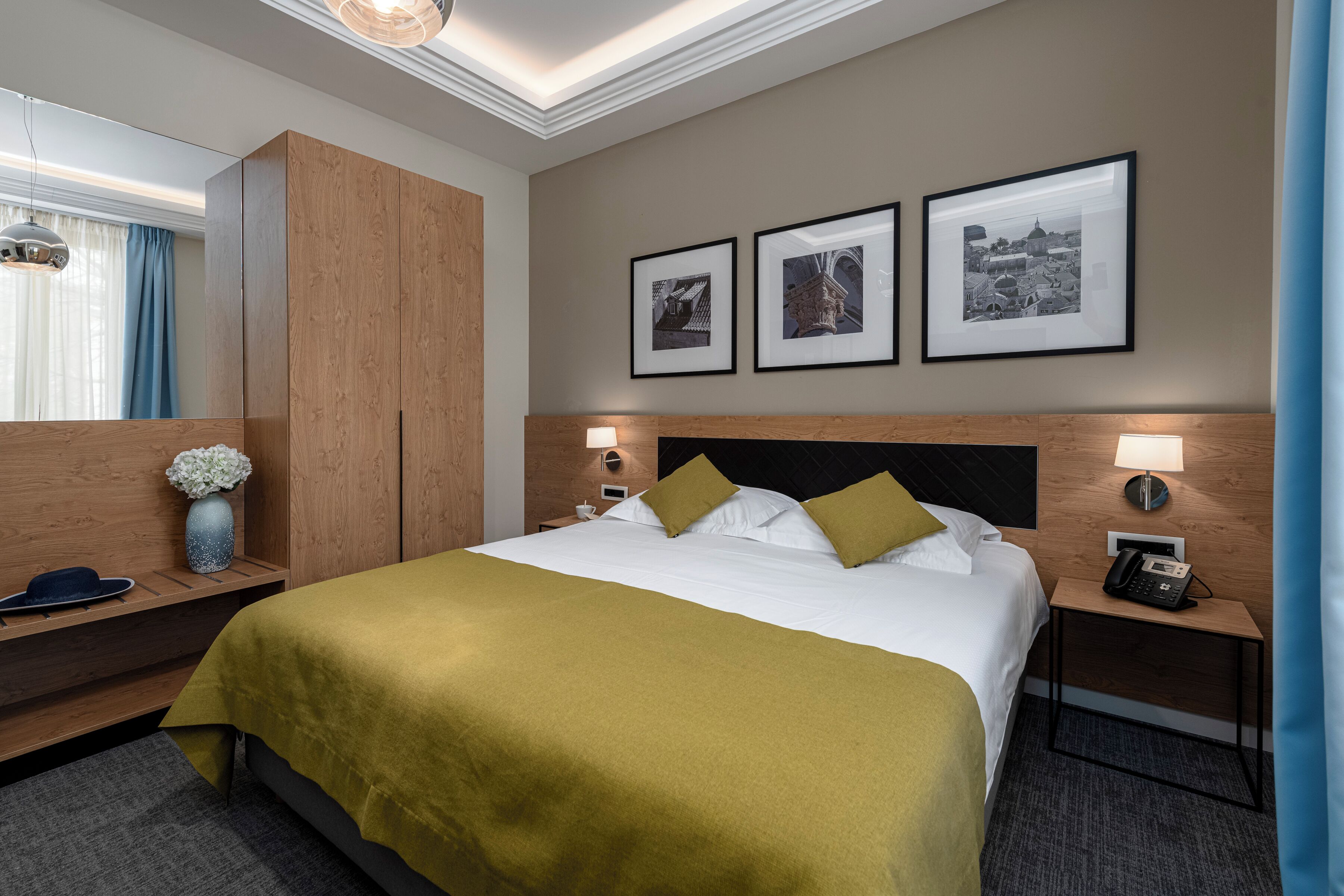Quarto de hotel com uma cama, duas mesas de cabeceira, um espelho e três quadros na parede.