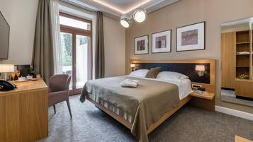 Quarto de hotel com cama, mesas de cabeceira, escrivaninha com telefone, cadeira e uma janela grande com cortinas.