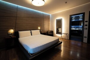 Quarto moderno com cama grande, mesas de cabeceira, uma cadeira e uma estante embutida para TV.
