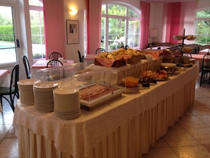 Disposição de buffet com diversos alimentos e pratos empilhados.