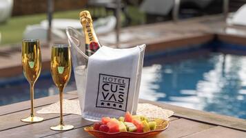 Mesa à beira da piscina com uma garrafa de champanhe, duas taças e uma cesta de frutas.