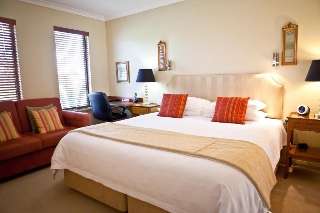 Quarto de hotel com uma cama grande, um sofá vermelho, uma escrivaninha com abajur e um espelho na parede.