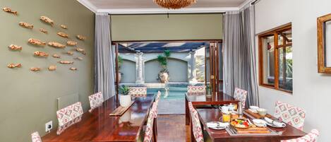 Uma sala de jantar com vista para a piscina, móveis de madeira e arte decorativa de peixes na parede.