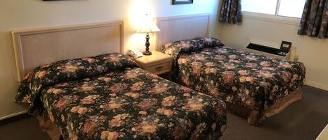 Quarto de hotel com duas camas, uma mesa de cabeceira com abajur, telefone e uma janela com cortinas.