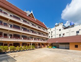 Um hotel de vários andares com telhado de telhas vermelhas, varandas e um estacionamento com dois carros.