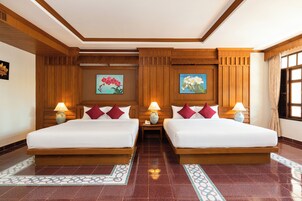 Quarto de hotel com duas camas, cabeceiras de madeira, uma janela grande com cortinas e piso ladrilhado.
