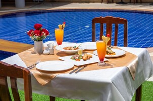 Mesa de jantar com pratos, talheres e bebidas à beira da piscina.