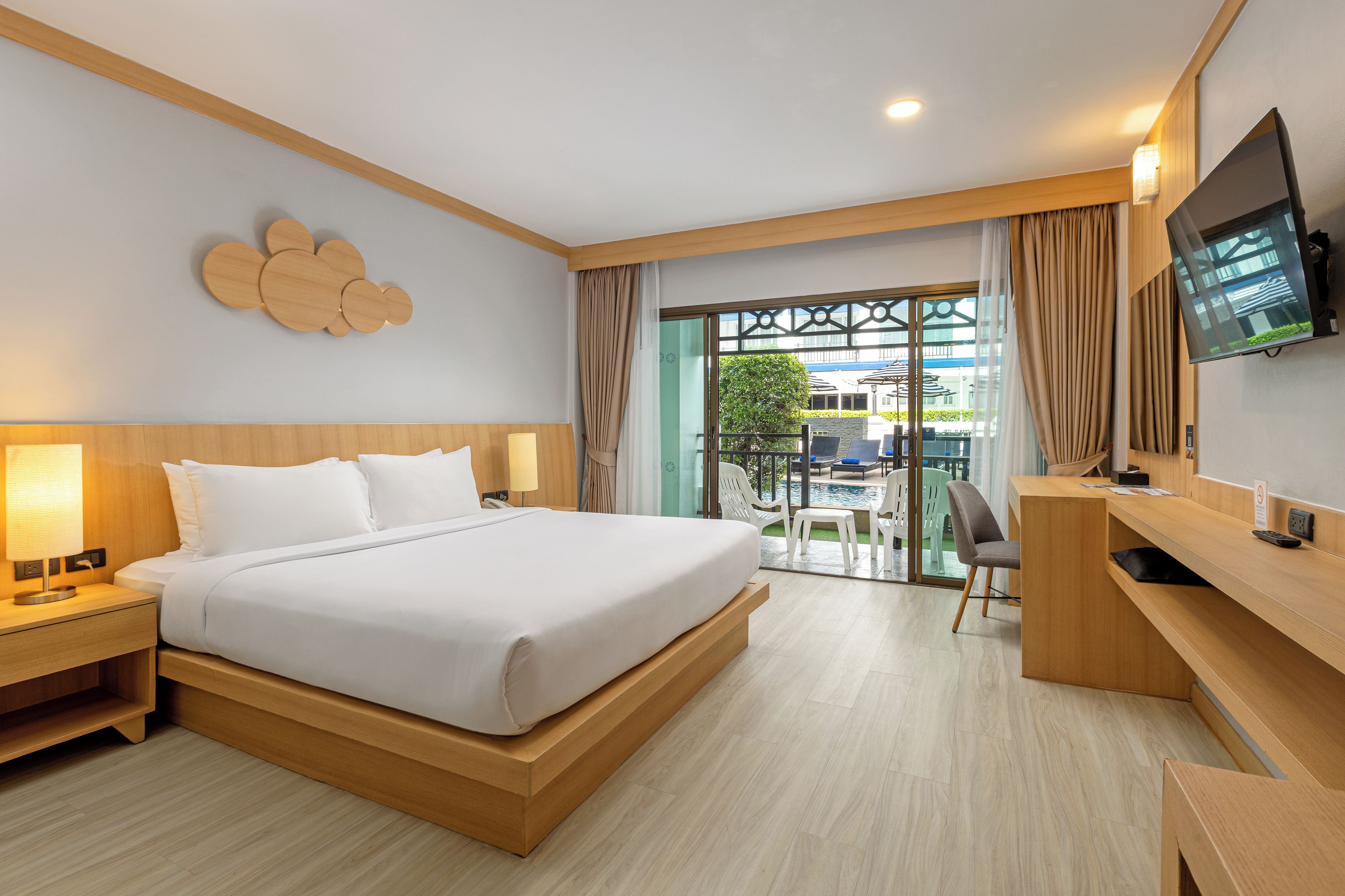 Quarto de hotel com cama, escrivaninha, TV e vista para a área externa.