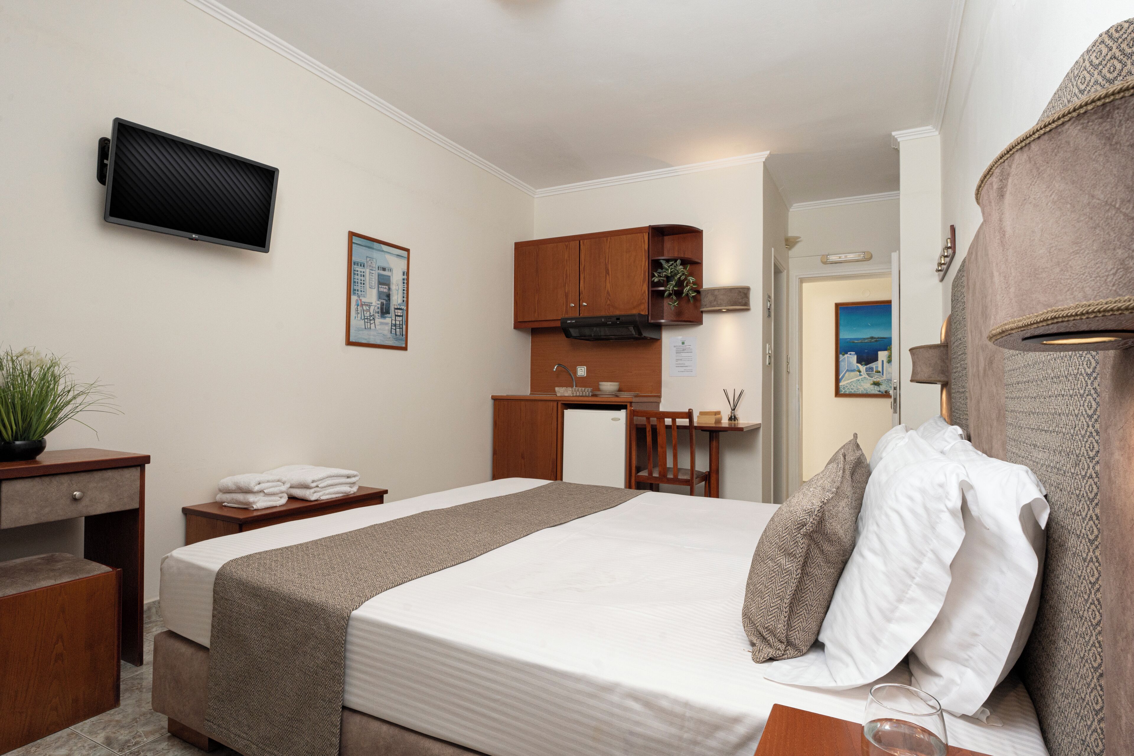 Quarto de hotel com cama, televisão presa na parede, cozinha compacta e vista para a cidade.