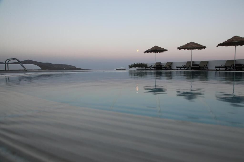 Uma piscina infinita com espreguiçadeiras e guarda-sóis, céu claro e vista distante do mar.
