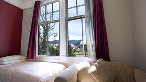 Quarto de hotel com duas camas, uma janela grande com cortinas e vista para uma paisagem com montanhas e vegetação.