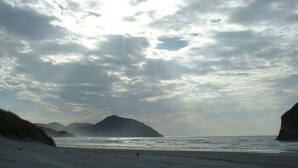 Uma praia com dunas de areia e uma montanha ao longe sob um céu nublado.