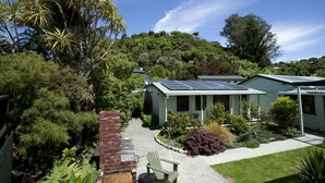 Uma casa com telhado solar, rodeada por vegetação exuberante e um muro de tijolos.