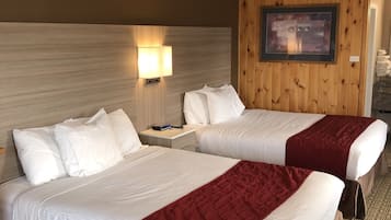 Quarto de hotel com duas camas, cabeceira de madeira, televisão montada na parede e mesa de cabeceira com abajur.
