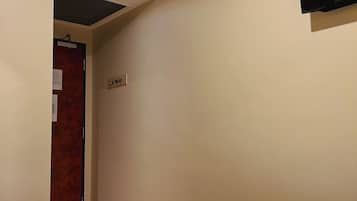 Quarto de hotel com uma cama, uma televisão fixada na parede e uma porta que dá para outro cômodo.