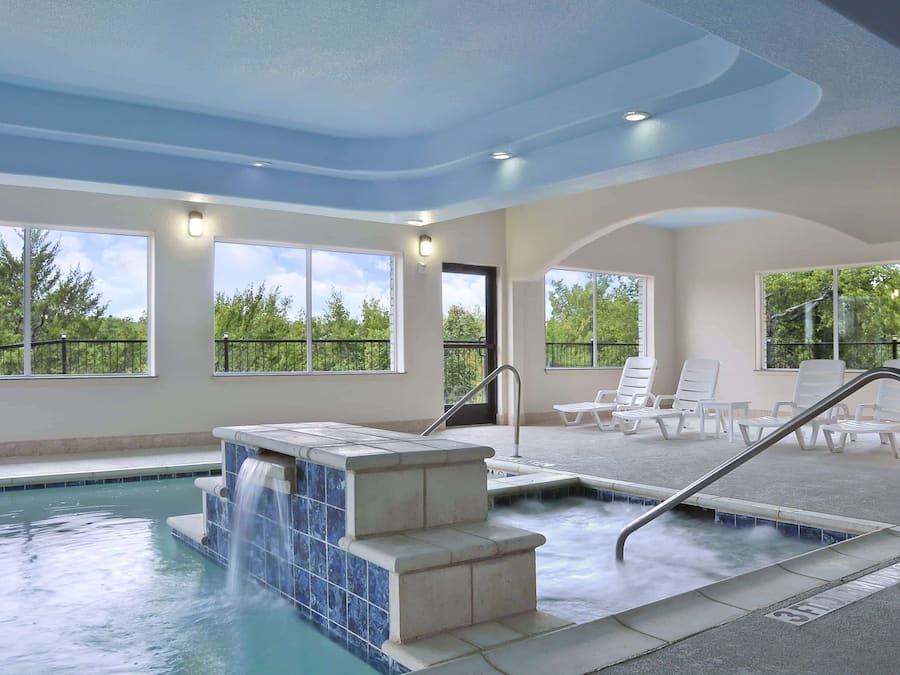 Área de piscina com hidromassagem, espreguiçadeiras e vista para árvores.