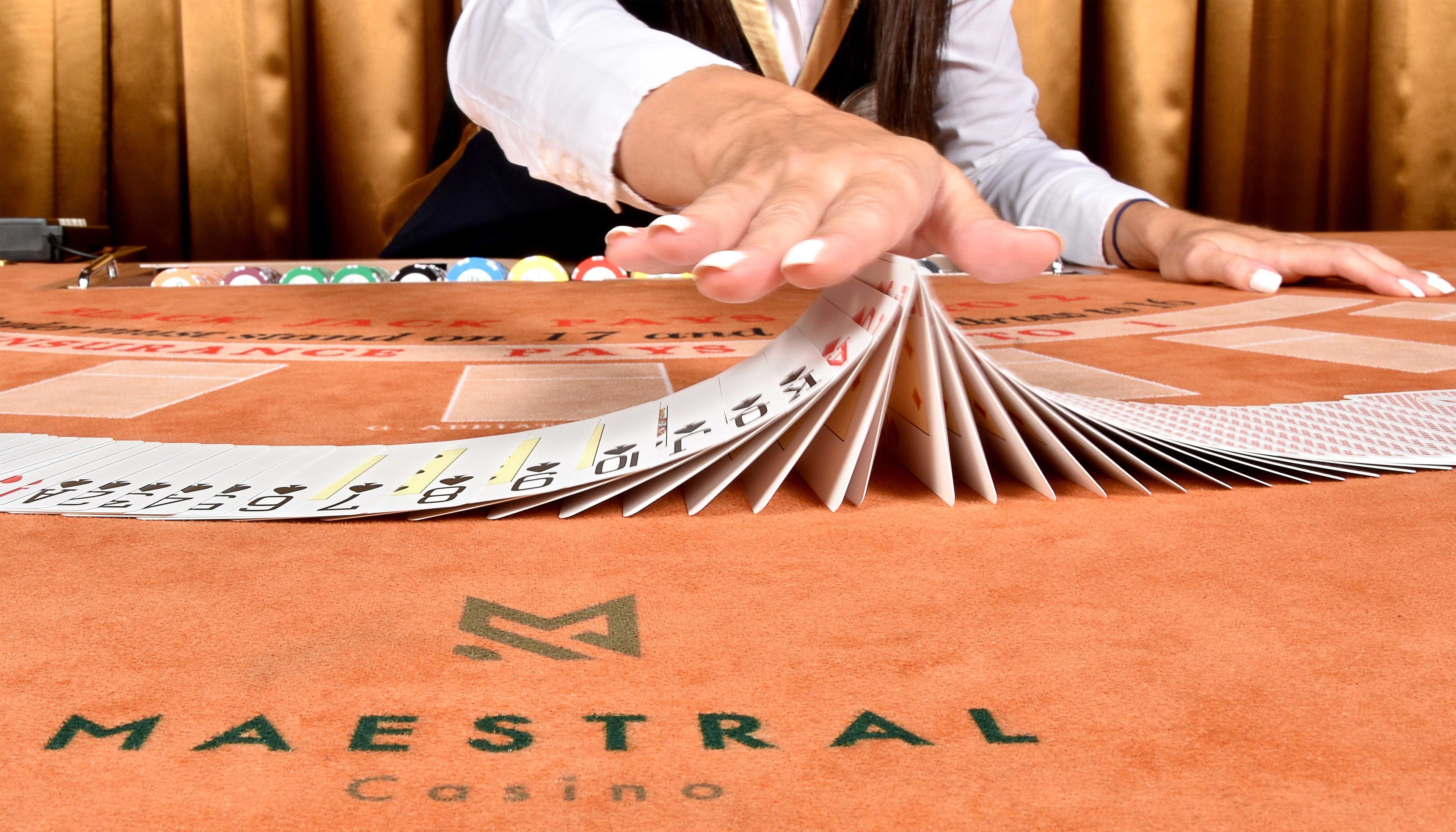 Uma pessoa embaralhando cartas em uma mesa com o logotipo 'MAESTRAL Casino'.