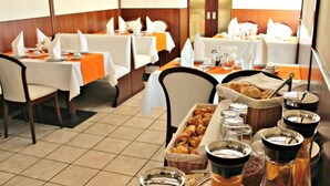 Disposição de buffet de café da manhã com mesas, cadeiras e diversos alimentos.