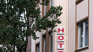 Um hotel com fachada rosa, entrada visível e uma placa com a palavra "HOTEL".