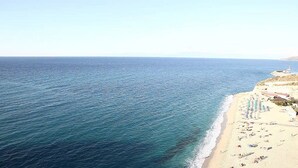 Uma praia costeira com areal arenoso e um farol ao longe.