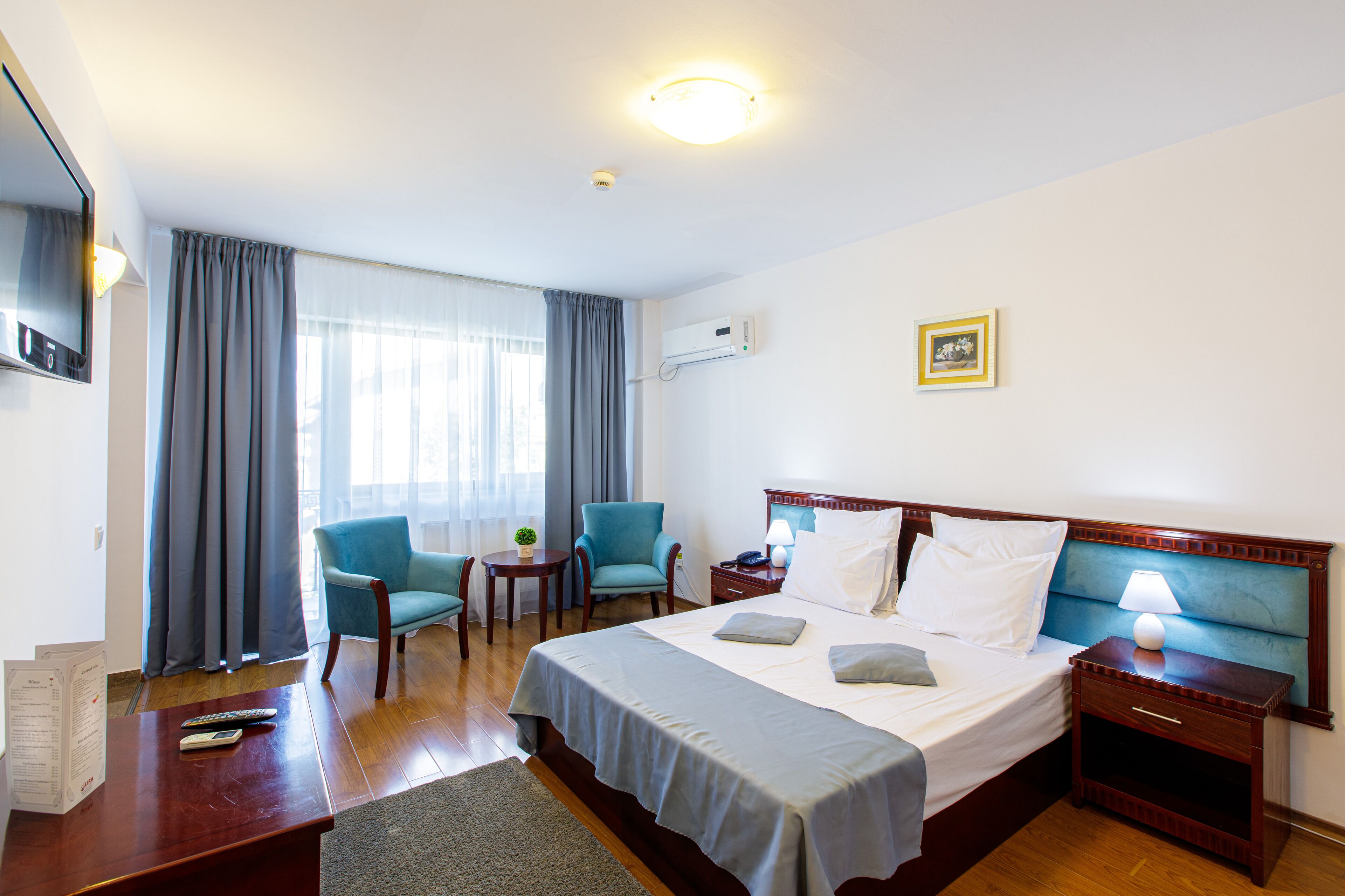 Quarto de hotel com cama, duas poltronas, uma mesinha, televisão e um quadro na parede.