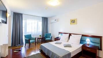 Quarto de hotel com cama, duas poltronas, uma mesinha, televisão e um quadro na parede.