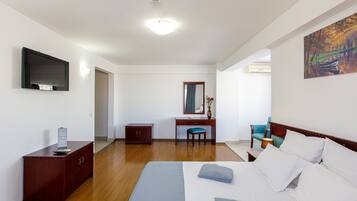Quarto de hotel com cama, escrivaninha, cadeira, televisão e um quadro na parede.