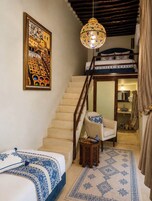 Quarto com cama de solteiro e beliche, uma cadeira, uma mesinha e luminária suspensa.
