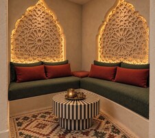 Um canto com assentos, incluindo um sofá, almofadas, tapete estampado e parede decorativa com desenhos elaborados.