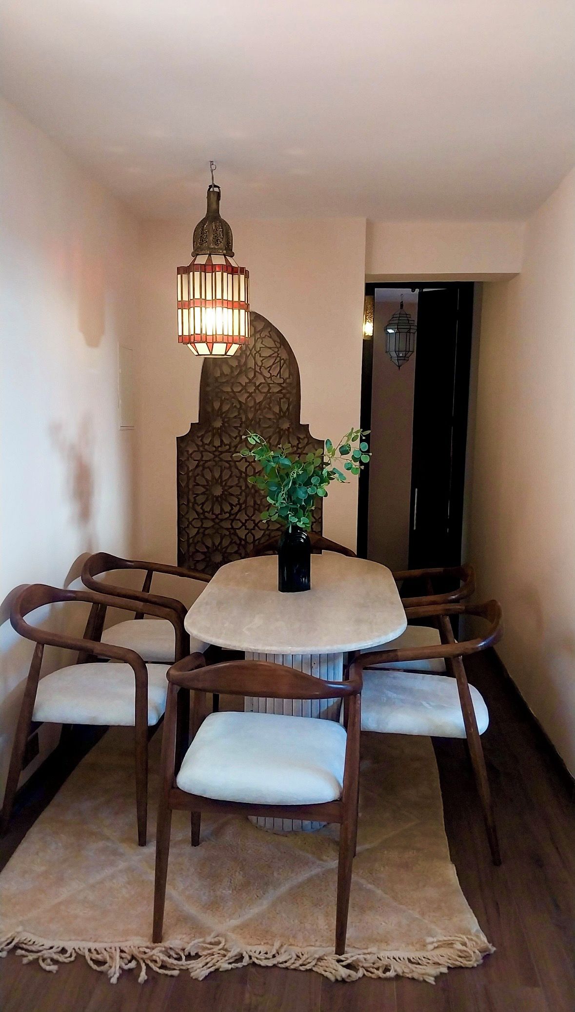 Uma sala de jantar com uma mesa redonda, quatro cadeiras, um vaso com plantas verdes e um lustre.