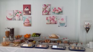 Mesa de buffet com diversos alimentos e pinturas de cupcakes decorativas na parede.