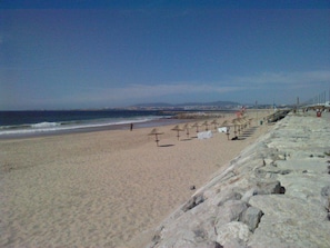 Uma praia com um molhe rochoso, guarda-sóis e uma vista clara do oceano.