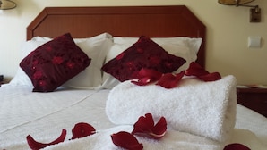 Uma cama bem arrumada com lençóis brancos e pétalas de rosa vermelhas espalhadas.