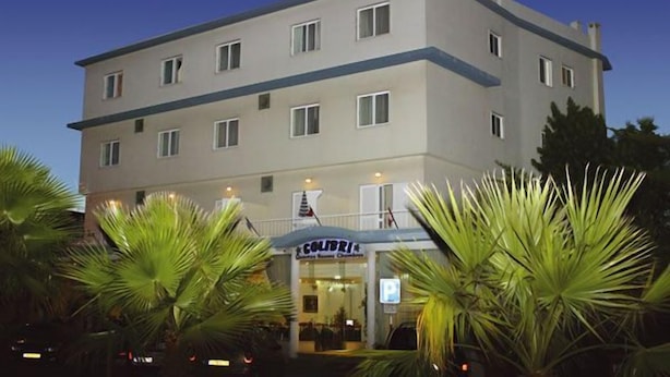 Um hotel com vários andares, fachada plana, restaurante no térreo e placa de estacionamento.
