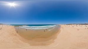 Uma praia com uma extensa área de areia, céu azul límpido e o oceano.