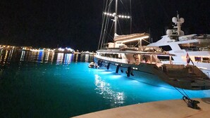 Um iate grande atracado em um porto noturno, com luzes brilhantes no mastro e no convés.